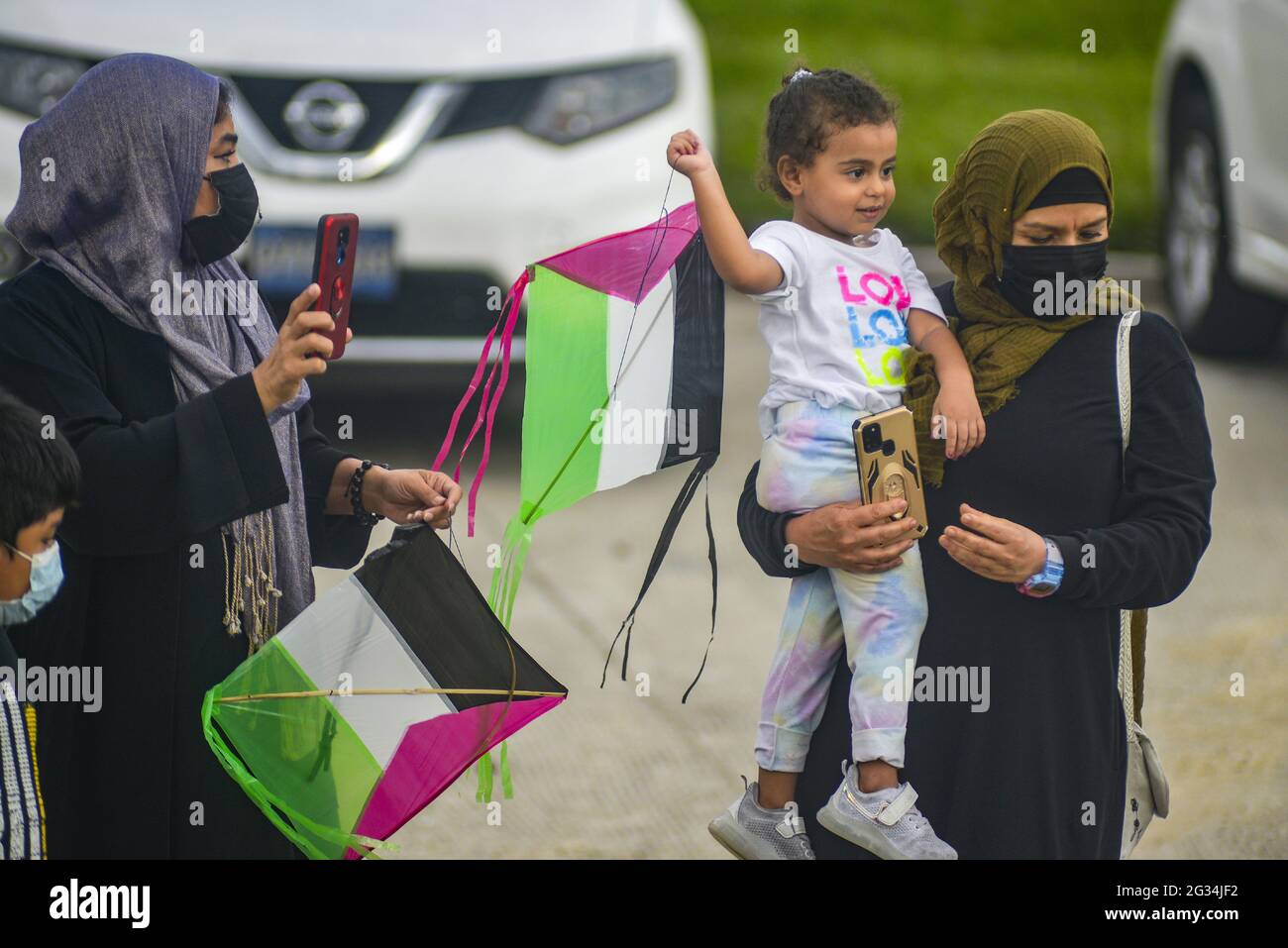 A woman wearing a hijab holds a kid playing with a kite displaying the ...