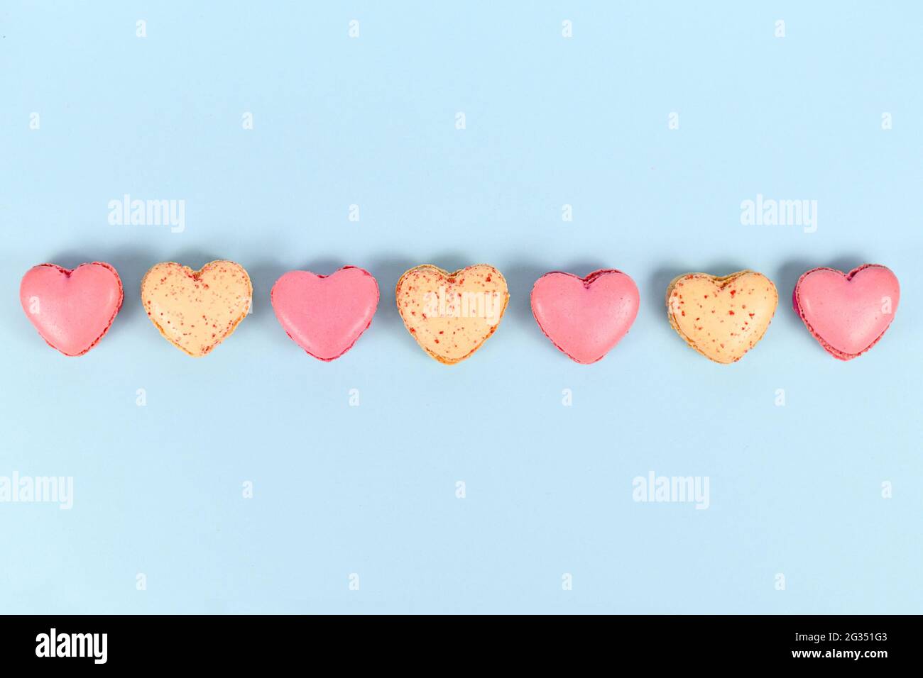 Pink and yellow heart shaped French macaron sweets in a row on blue ...