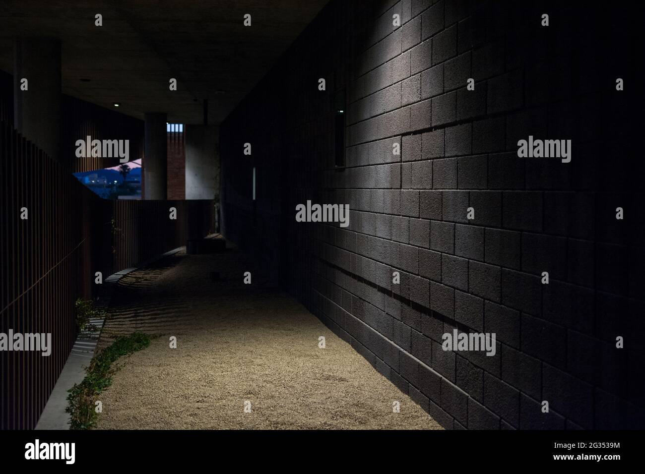 Alleyway along a brick wall and fence under light Stock Photo - Alamy
