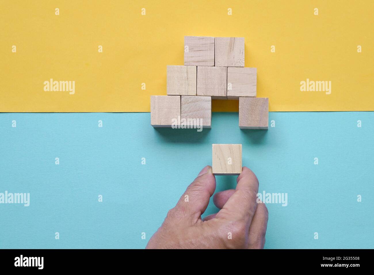 Man's hand inserting piece of wood block to complete a pyramid shape of ...
