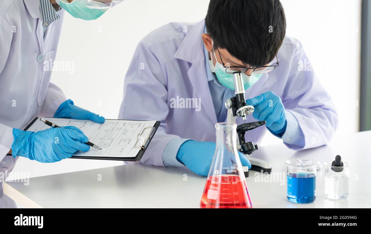 Attractive young scientist team in lab coat and safety goggles working ...
