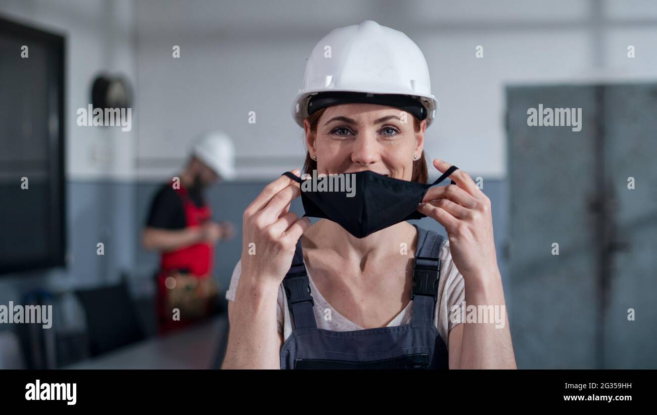 Portrait of woman worker with helmet indoors in factory putting on face ...