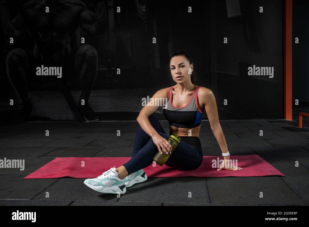 Athletic young woman sitting on mat in modern gym Stock Photo - Alamy