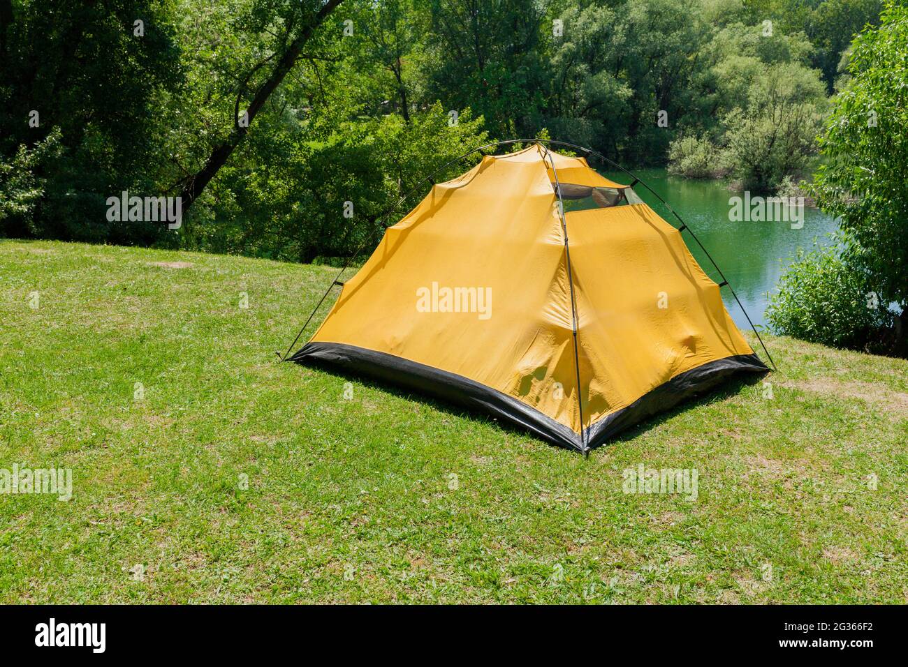 Yellow tent on a grass hill by the lake ready for camping Stock Photo ...