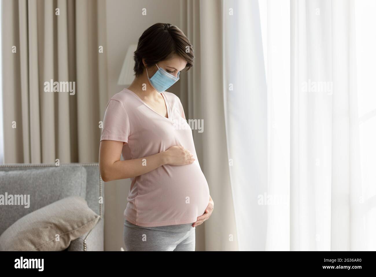 Pregnant woman wearing medical face mask, touching caressing belly ...