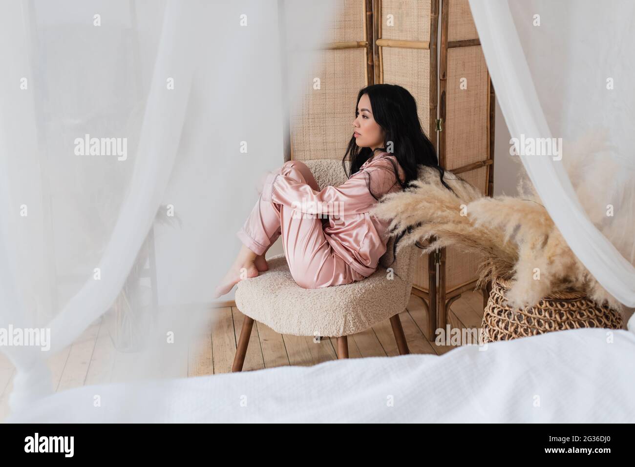 thoughtful young asian woman sitting on chair in self hug pose in ...