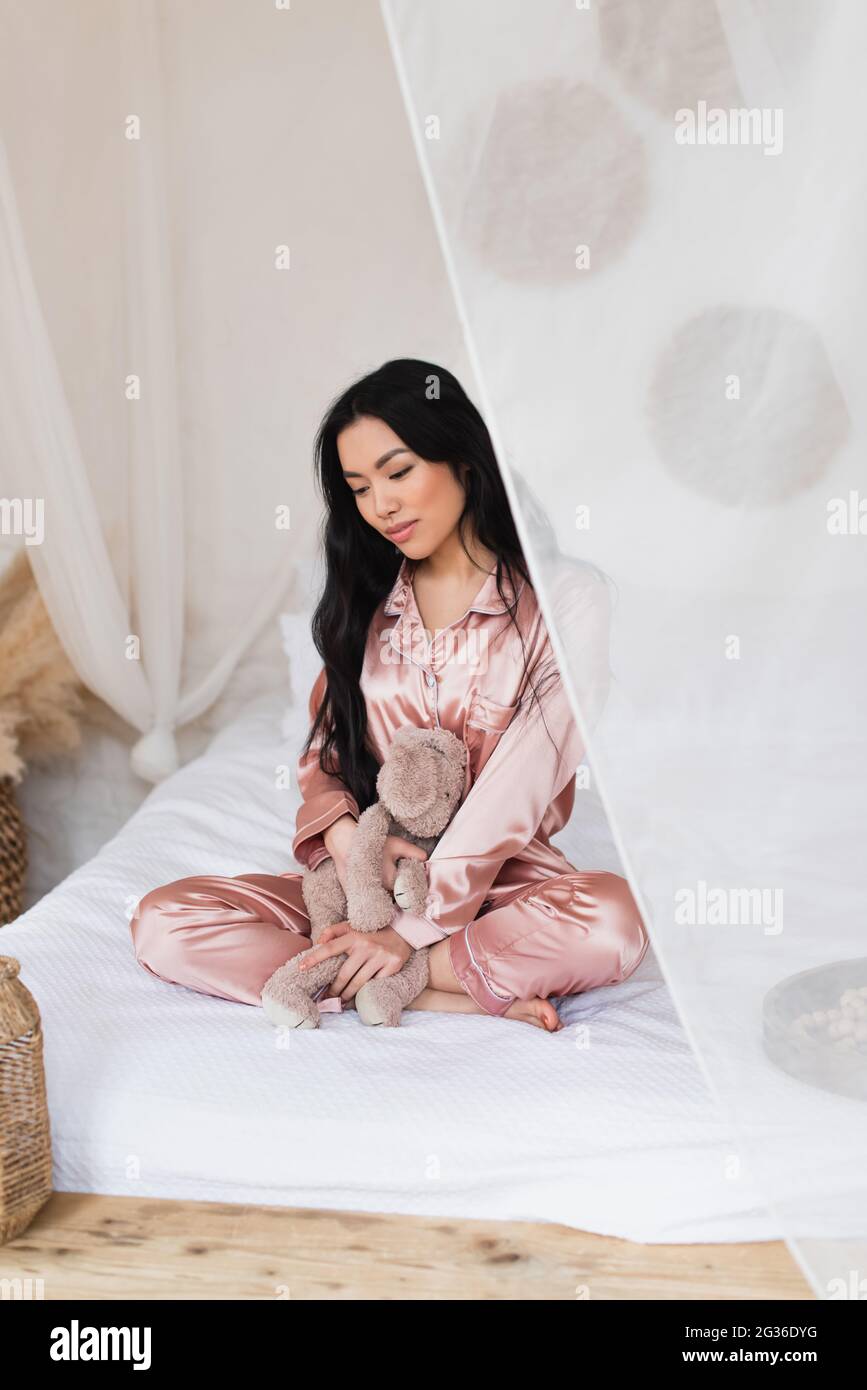 sad young asian woman in pink silk pajamas sitting with crossed legs on ...
