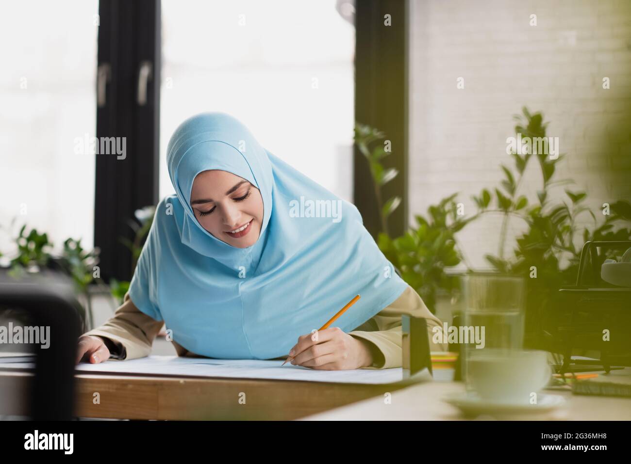 smiling arabian engineer in hijab drawing blueprint on blurred ...
