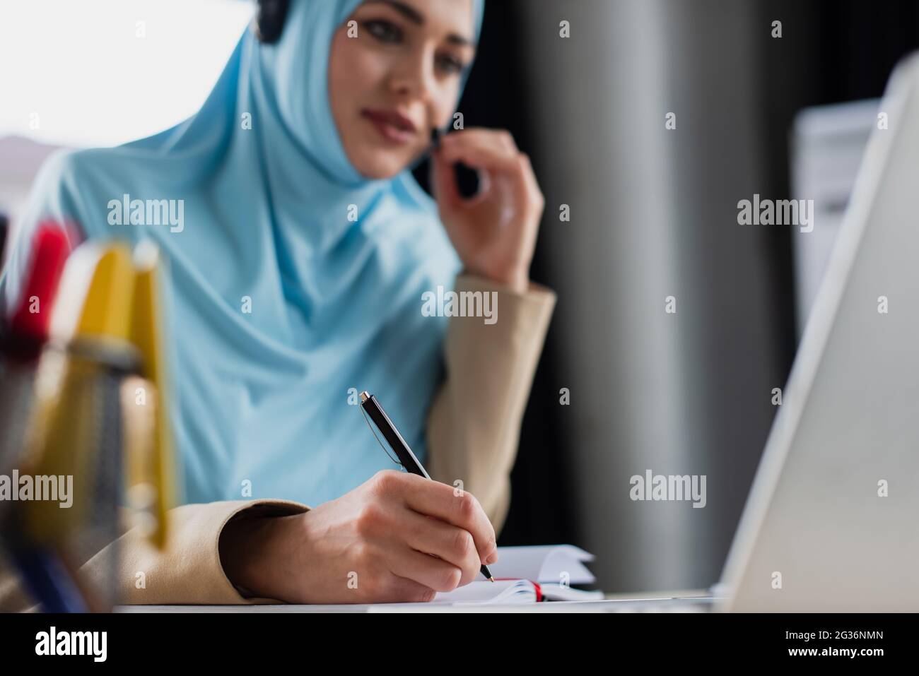 blurred muslim woman writing in notebook while working in call center ...