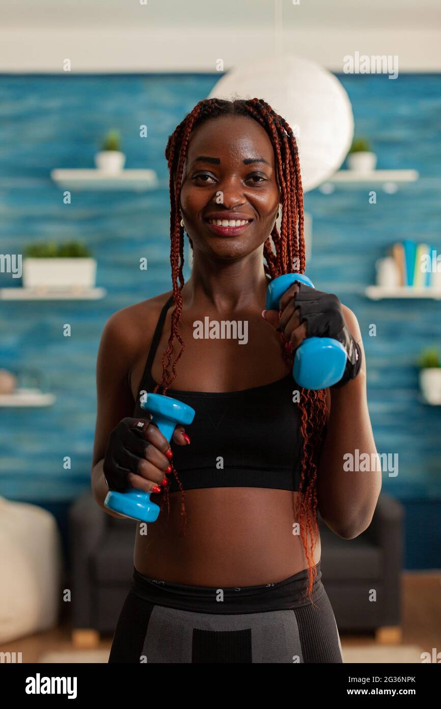 Fit black woman exercising biceps with dumbbells in home living room ...