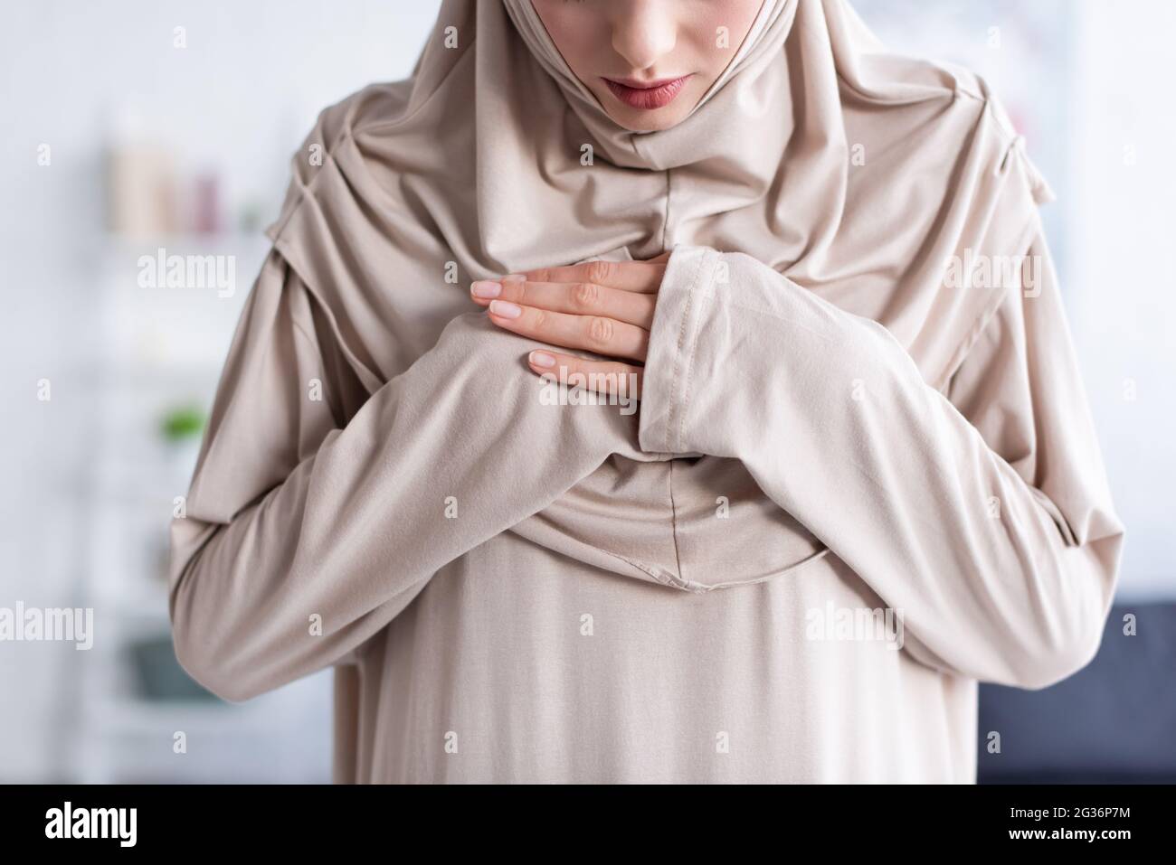 partial view of young muslim woman holding hands on chest while praying ...