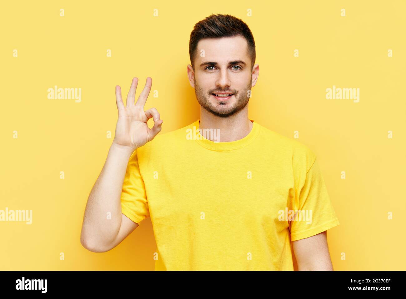Smiling handsome man doing ok sign with hand and fingers over yellow ...