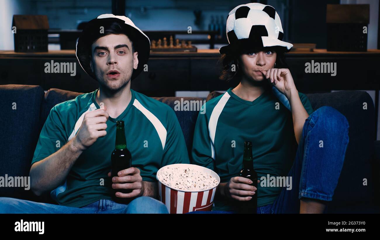 stressed football fans in fan hats holding bottles of beer and watching ...