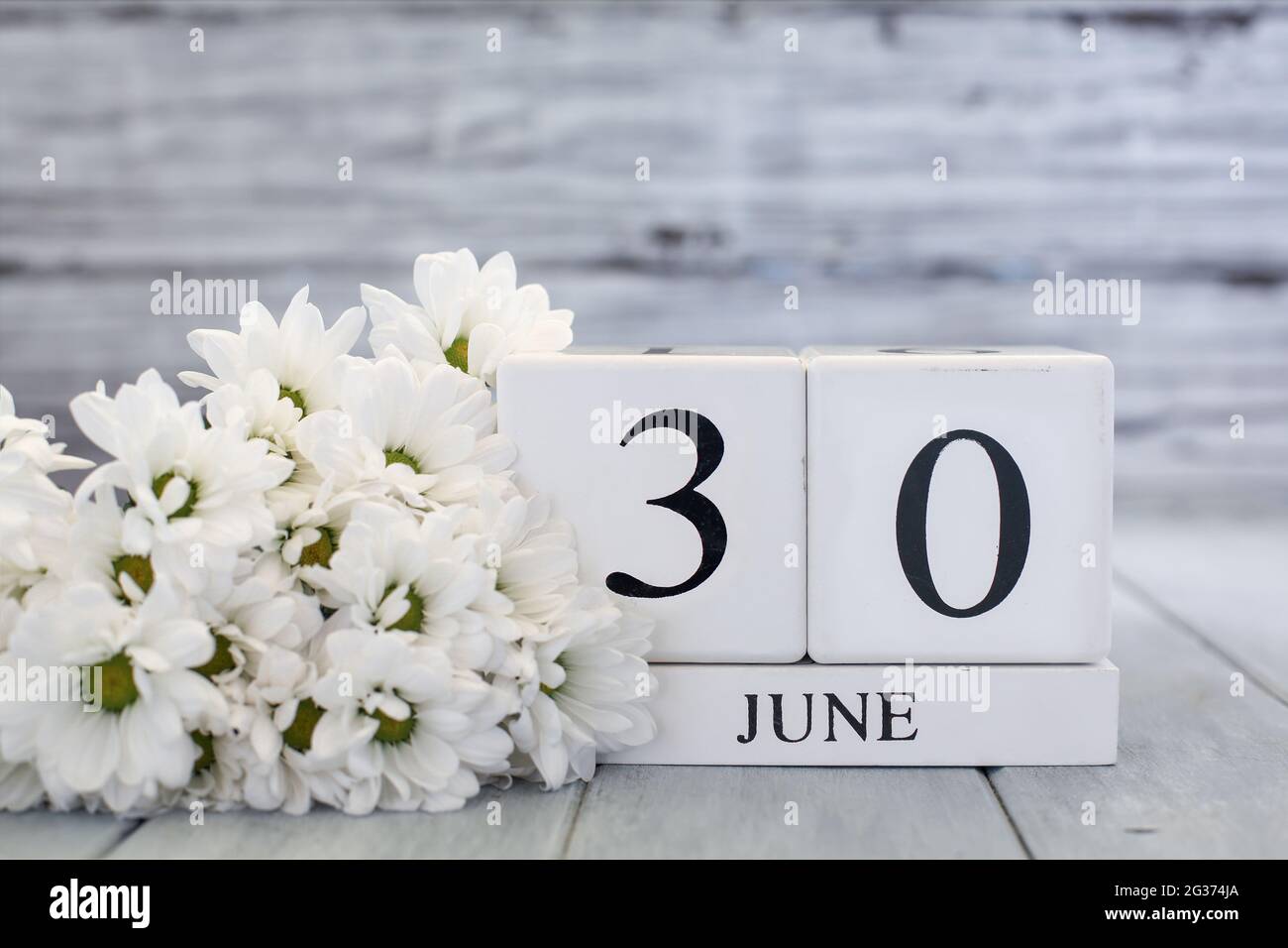 White wood calendar blocks with the date June 30th and white daisies ...