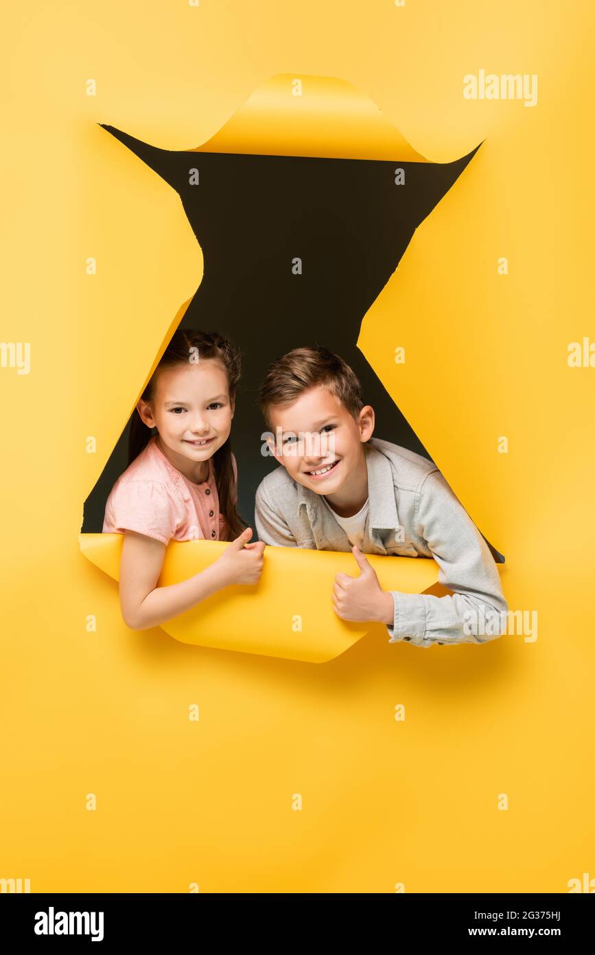 happy kids showing thumbs up and looking at camera through hole on ...