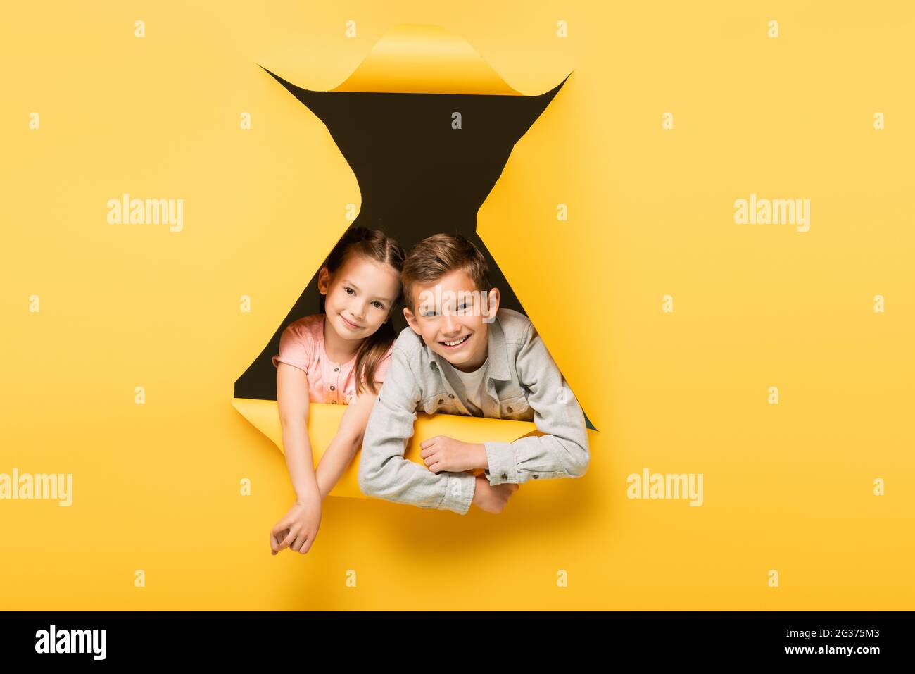 happy kids looking at camera through hole on yellow background Stock ...