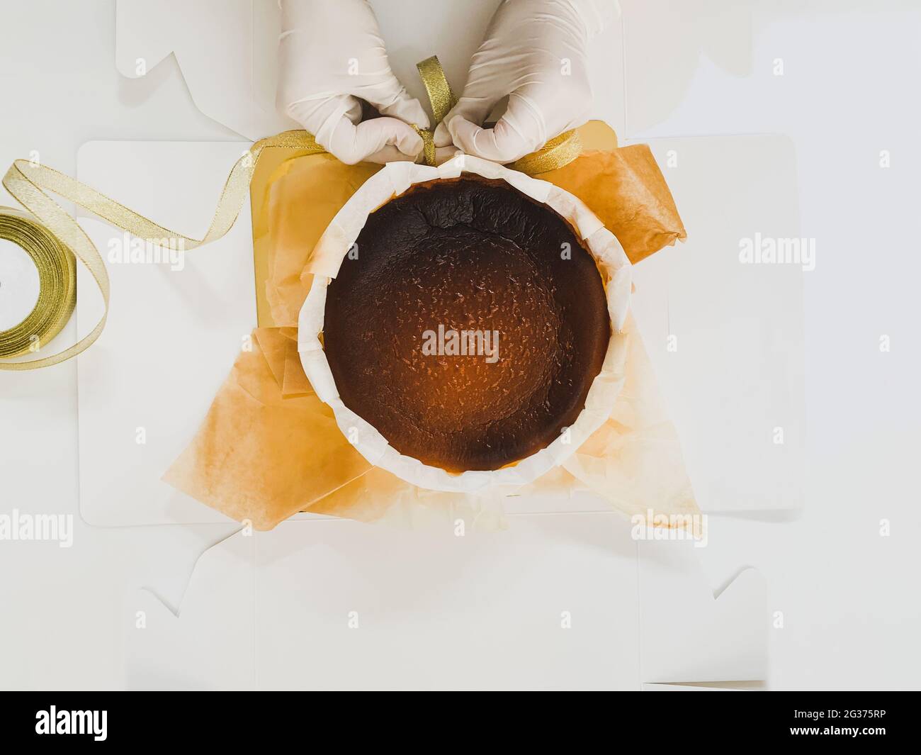 Female baker hand with glove packing basque burnt cheesecake cake with ...
