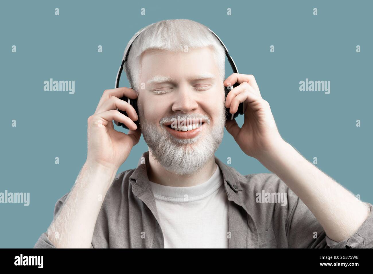 Happy albino man listening music in wireless headphones and touching ...