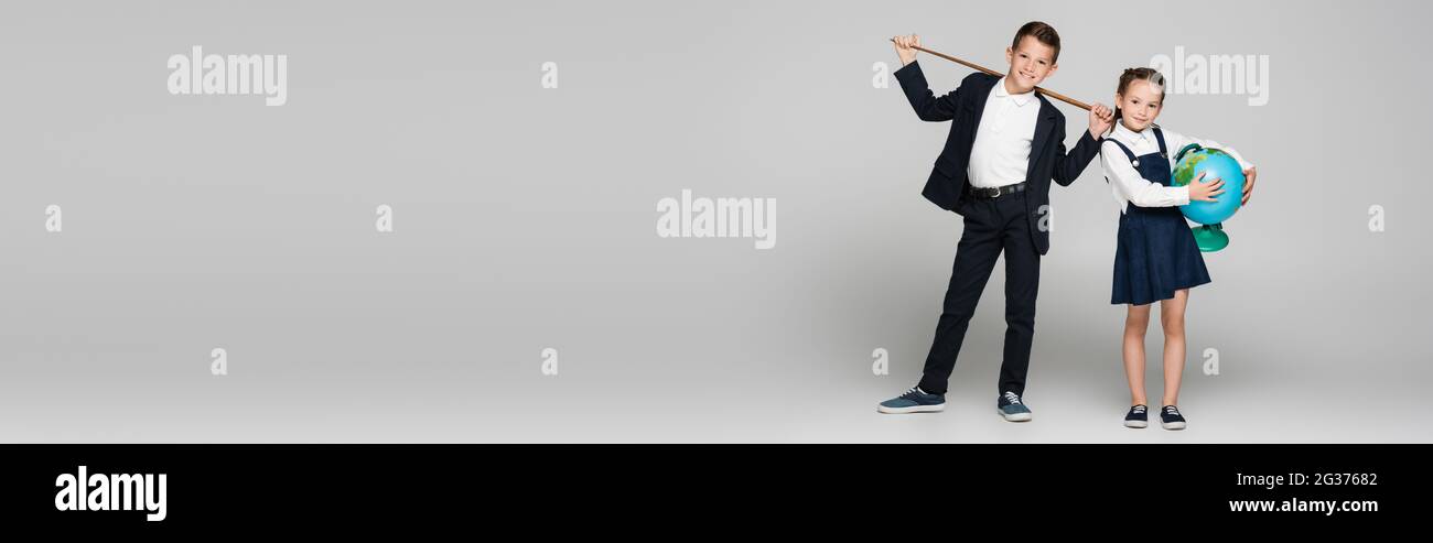 happy schoolboy holding pointing stick near girl in dress with globe on ...