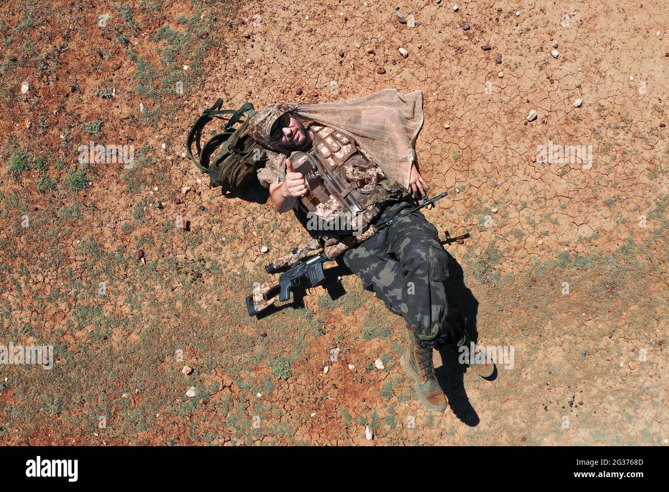 A soldier sniper while resting. He lies on the red-hot desert ground ...