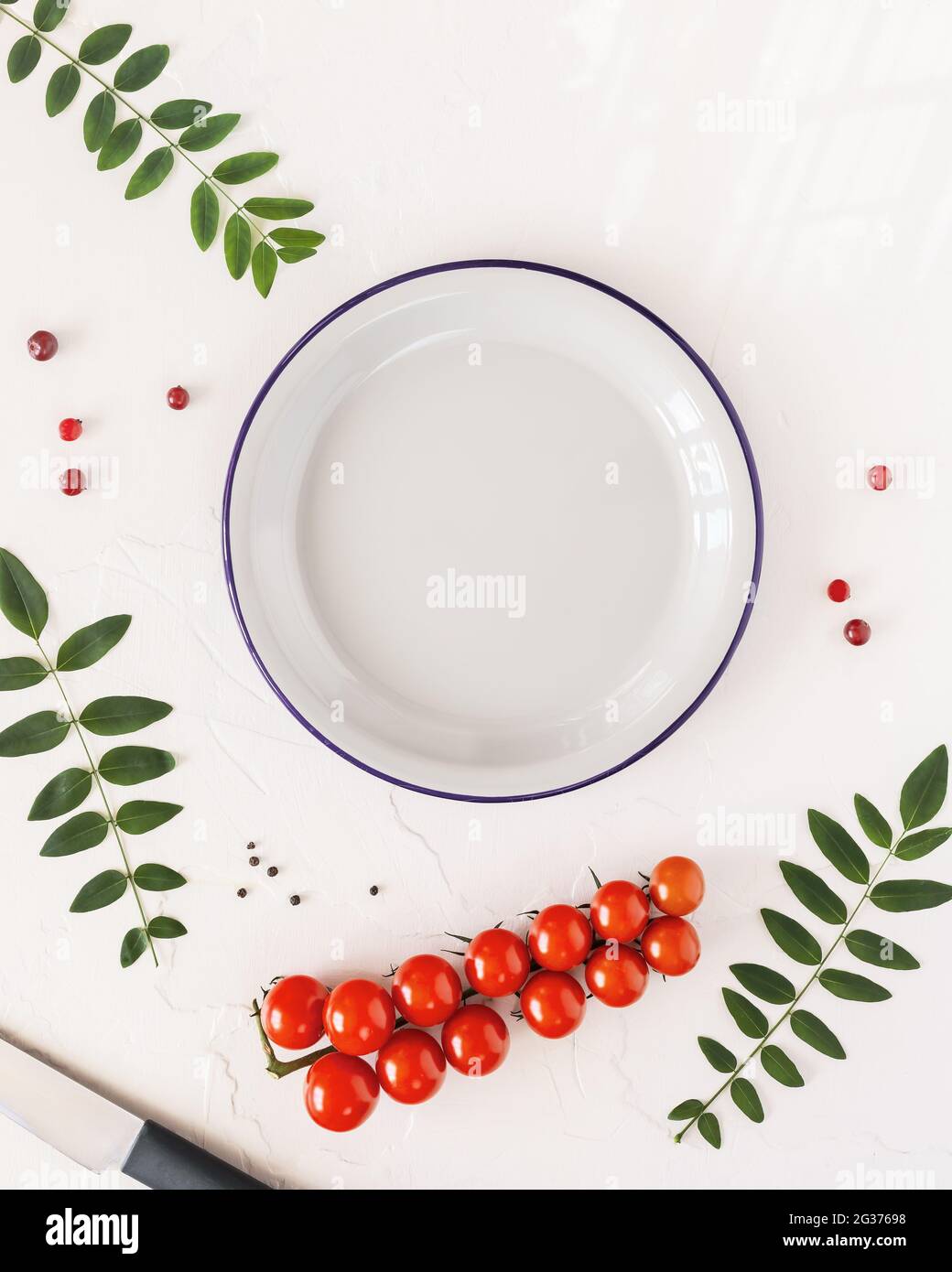 Vertical food composition with empty white plate, tomatoes, herbs and ...