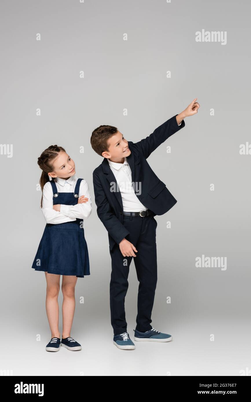 girl in dress standing with crossed arms near boy pointing with finger ...