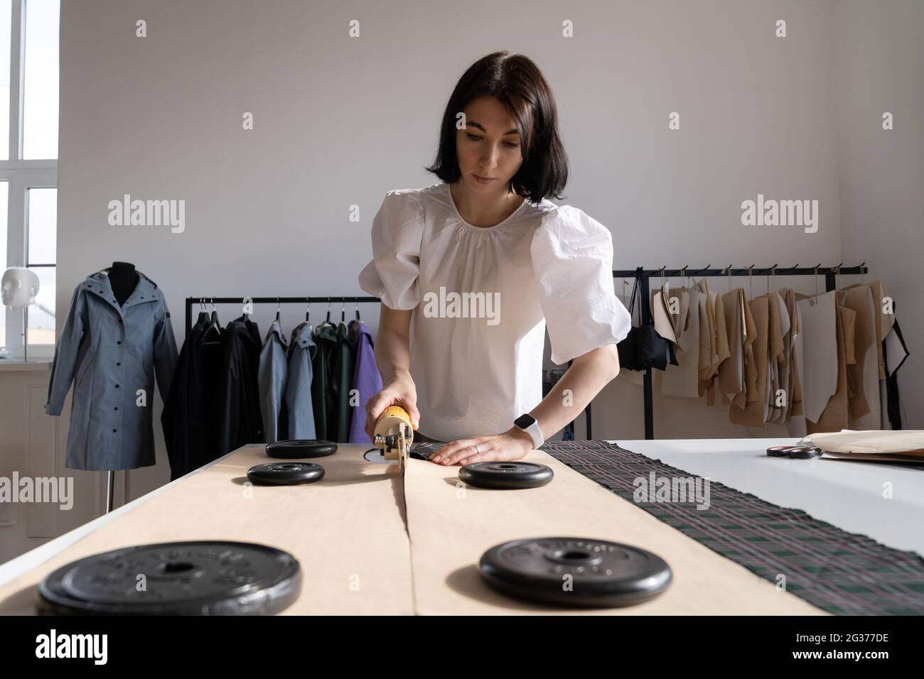 Designer at work woman tailor cut cloth material with electric cutter ...