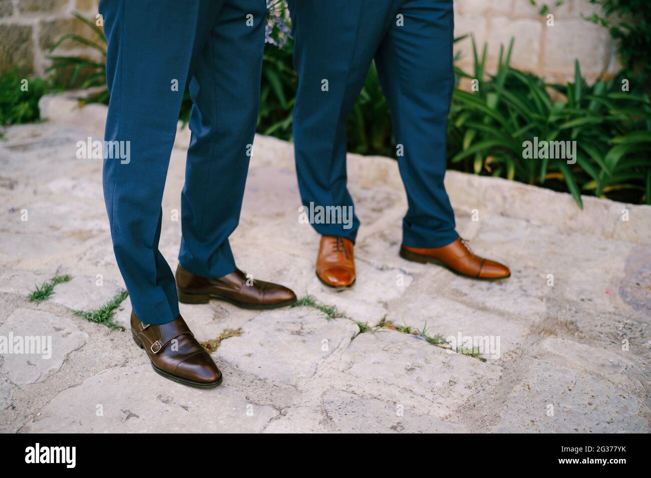 The legs of two men standing on a cobbled road, close-up. The groom and ...