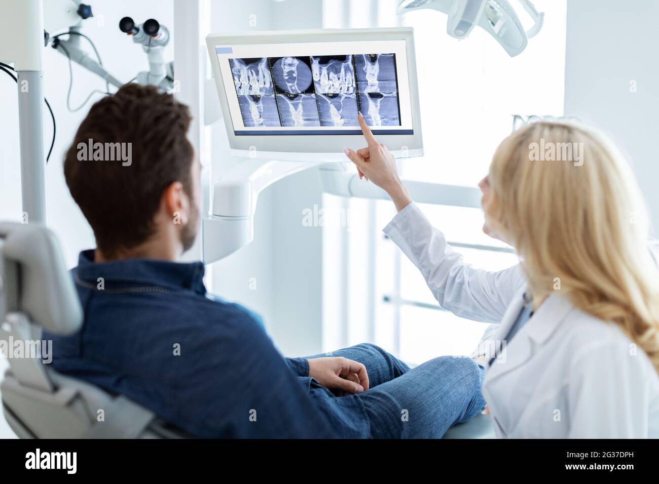 Woman dentist having conversation with patient, poitning at LED display ...