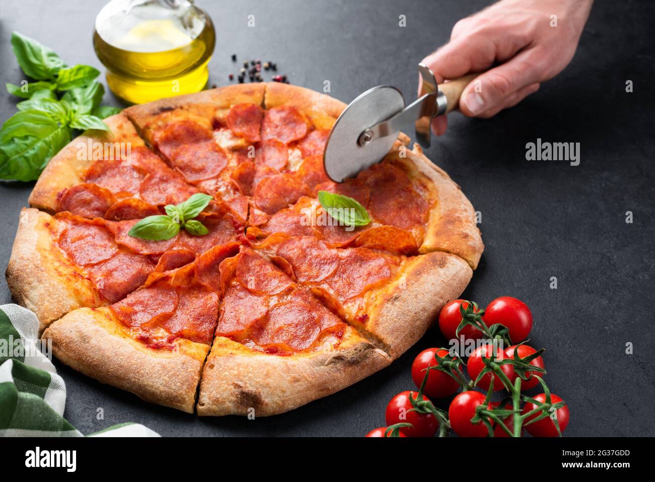 Hand slicing pepperoni pizza on black concrete background. Tasty hot ...