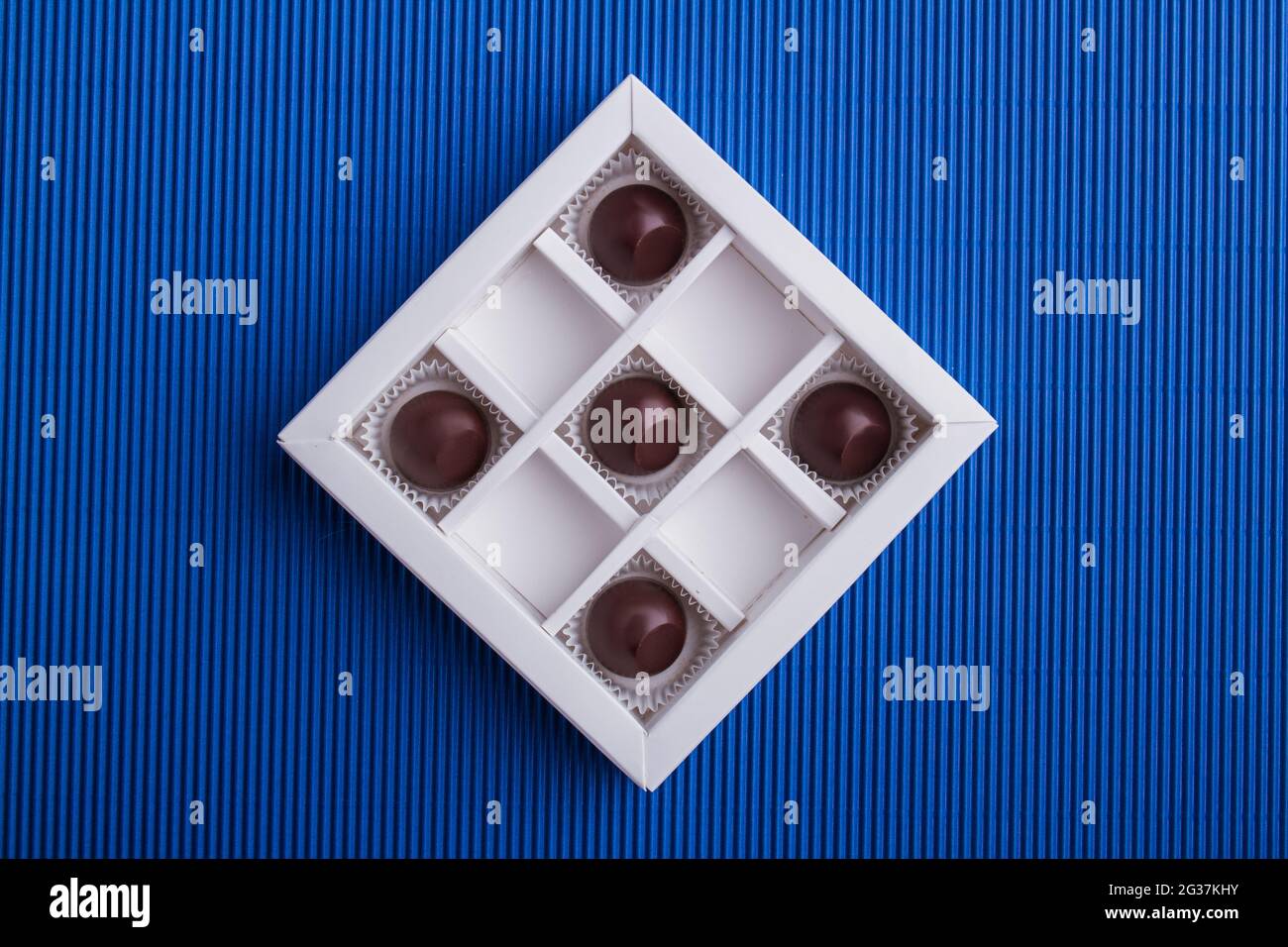 Five brown chocolate candies in the box on blue background Stock Photo ...