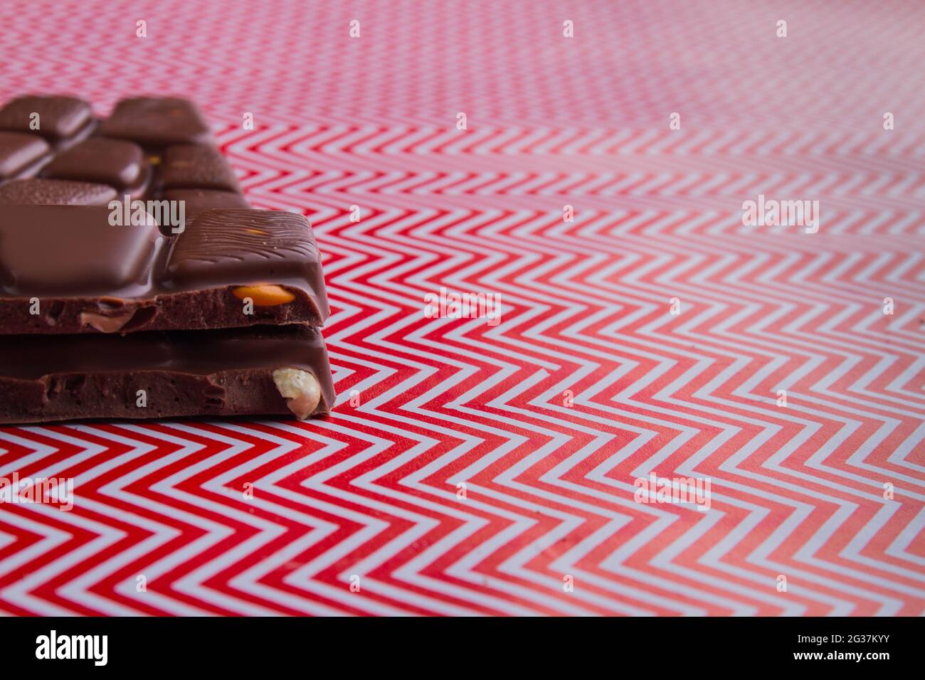 Close-up cut chocolate bar pieces with nuts on red and white background ...