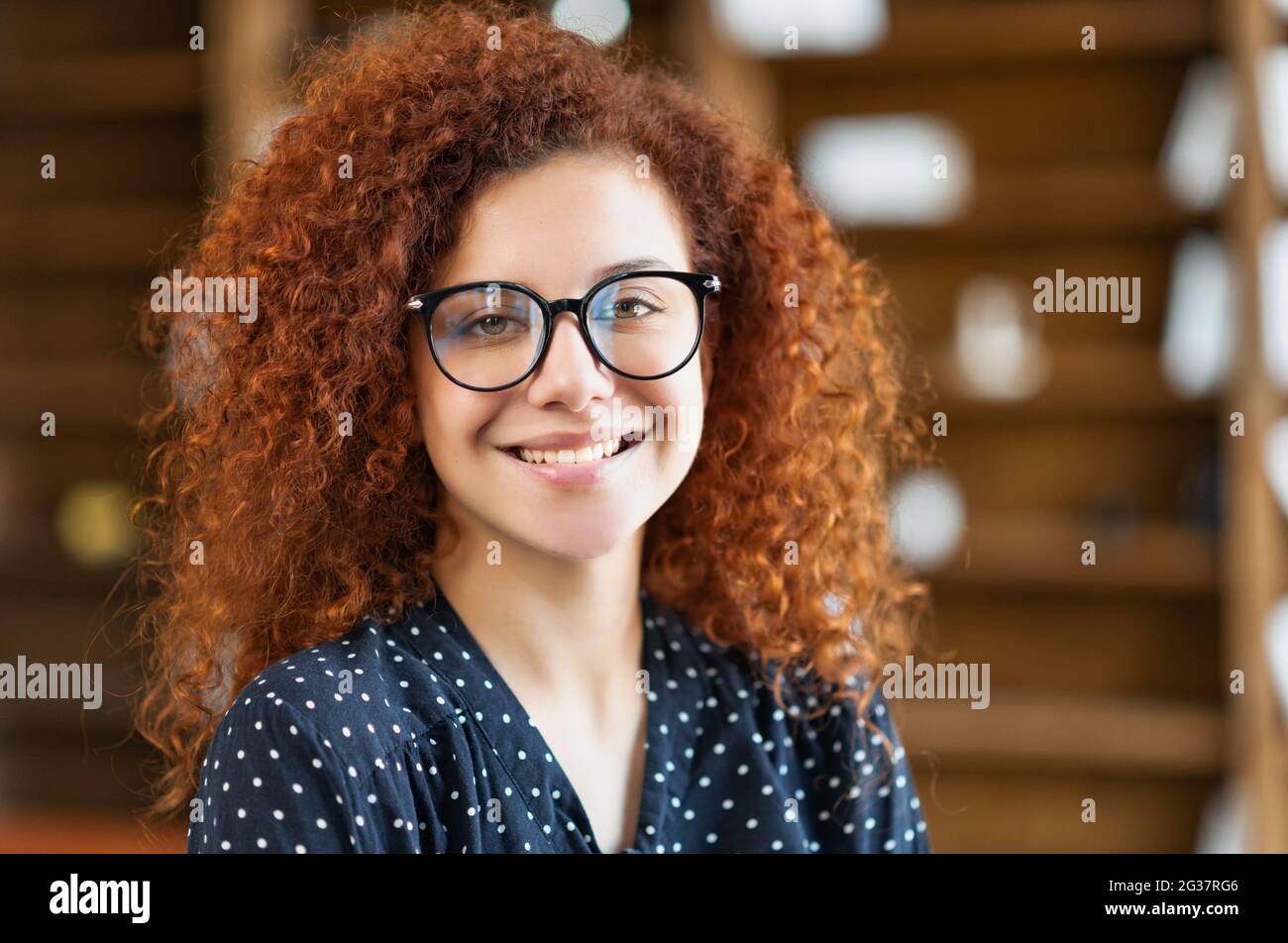 Headshot of young elegant female employee with curly ginger hairstyle ...