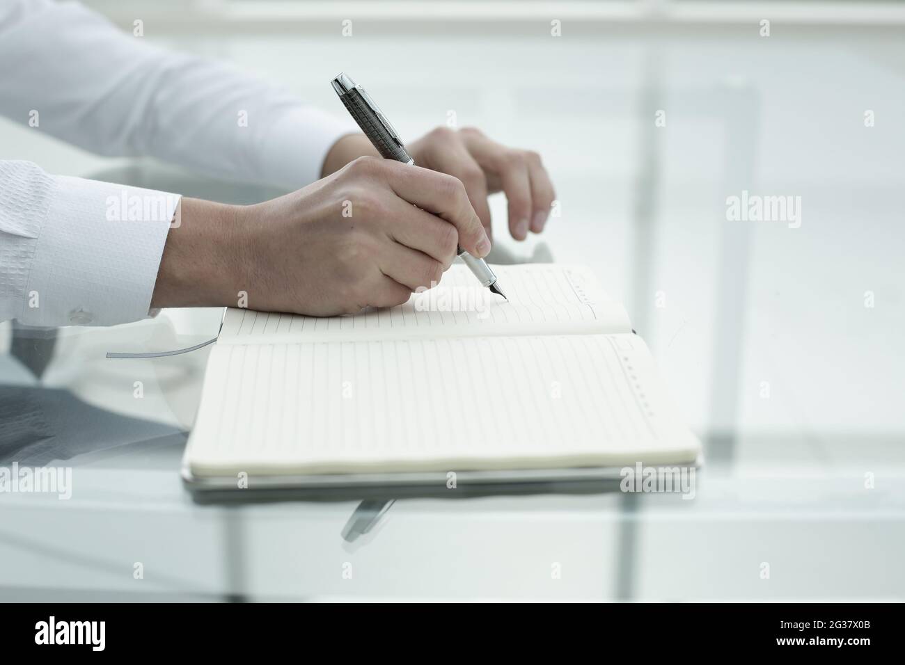 Office worker's hand writes in notebook behind a glass table Stock ...