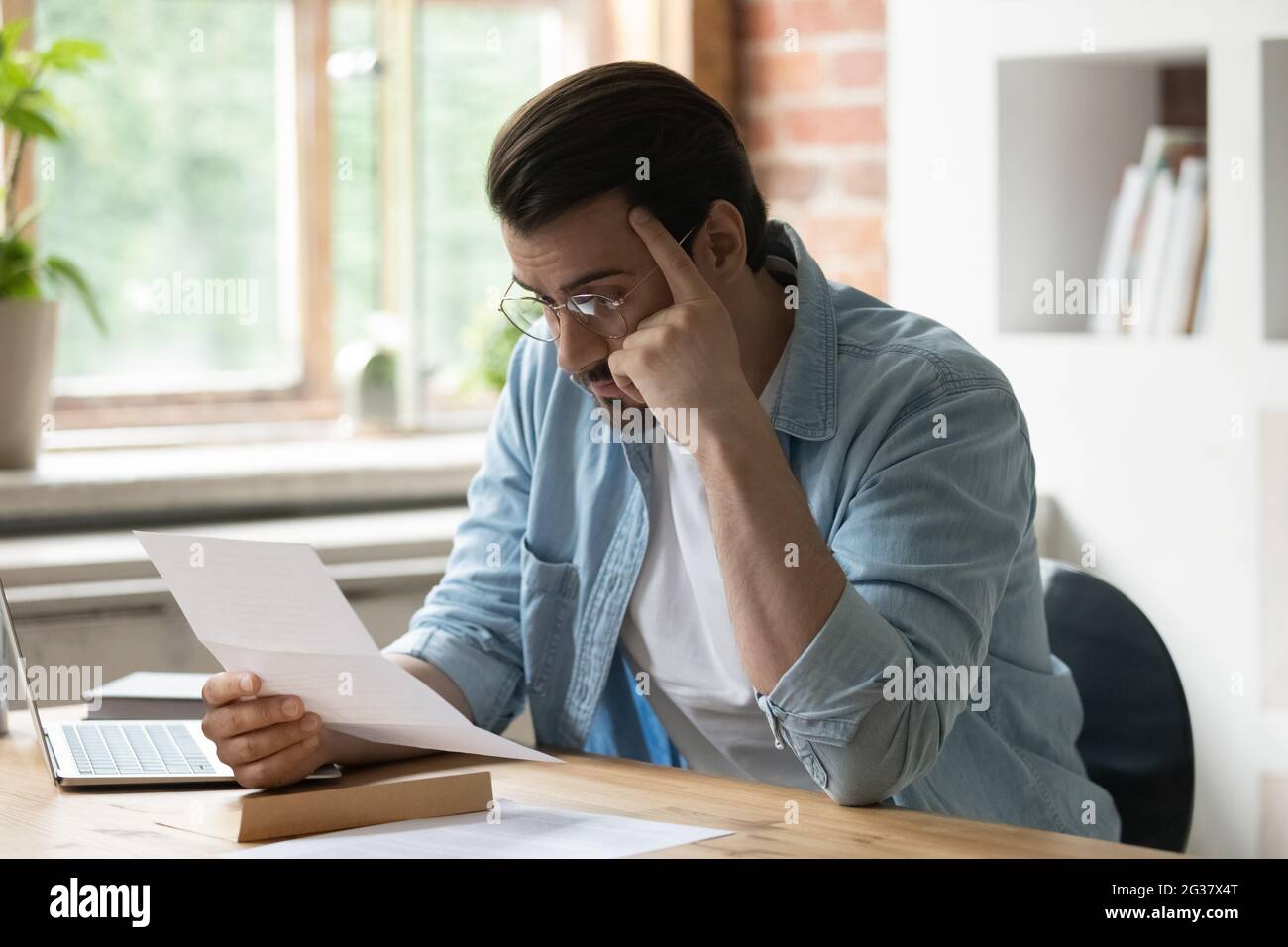 Stressed young man reading paper letter with bad news Stock Photo - Alamy