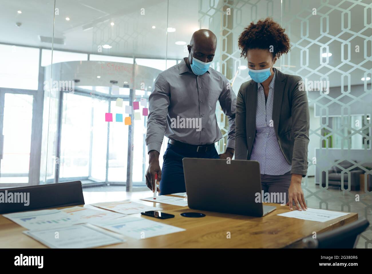 Two diverse male and female business colleagues wearing face masks and ...