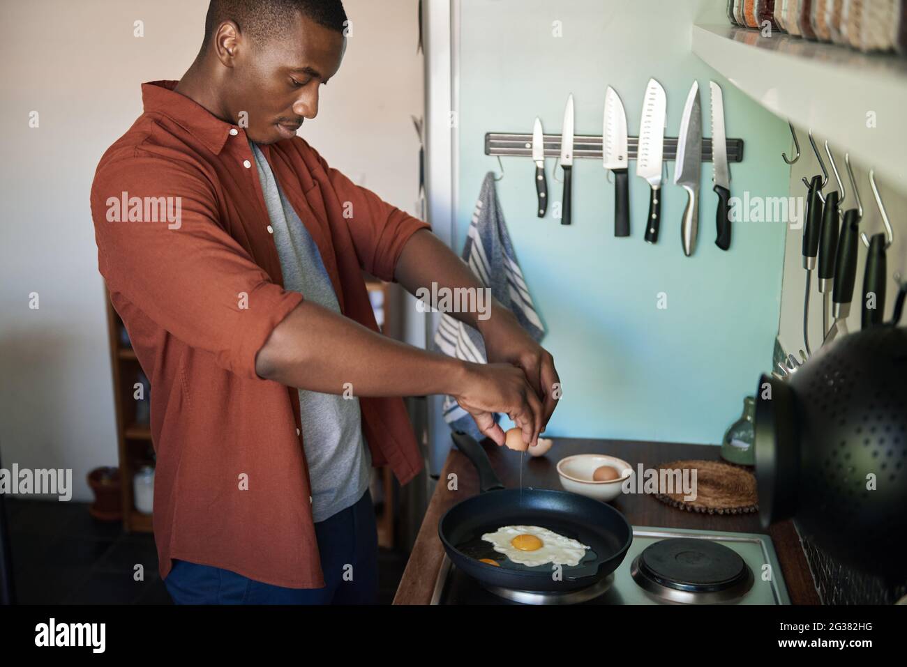 Young African man cracking eggs into a frypan for breakfast Stock Photo ...
