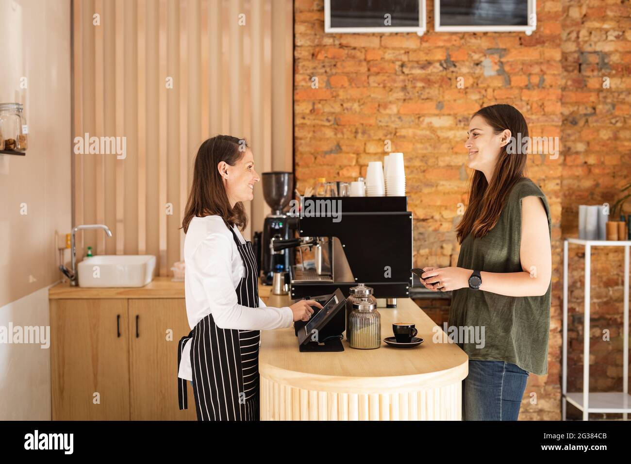 Two caucasian female business owner and customer standing at countertop ...