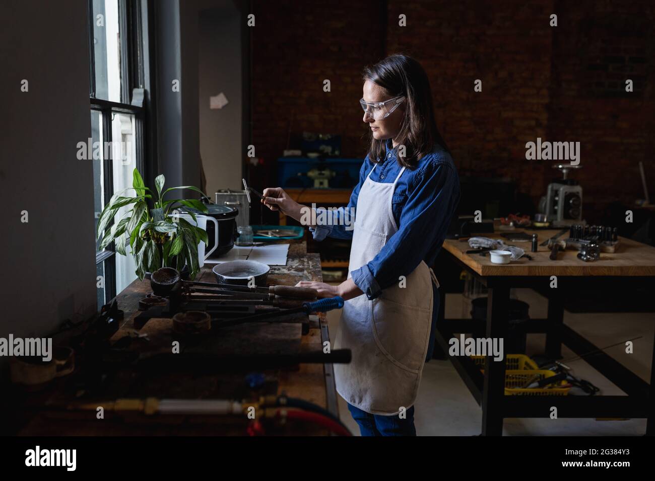 Caucasian female jeweller wearing apron and glasses, preparing ...