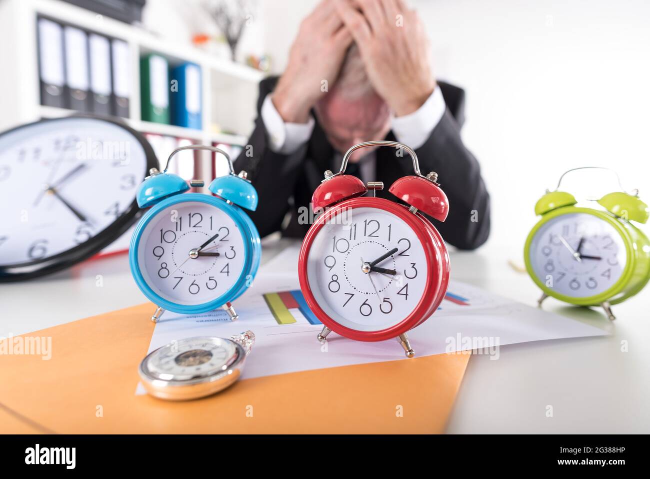 Stressed businessman behind his desk full of alarm clocks Stock Photo ...