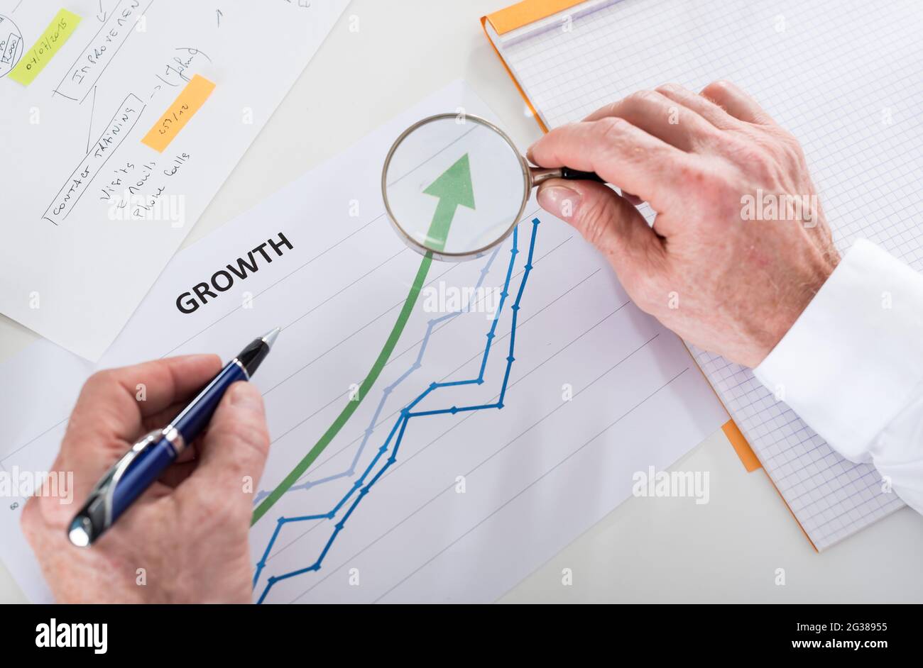 Businessman holding a magnifying glass over a graph showing growth ...