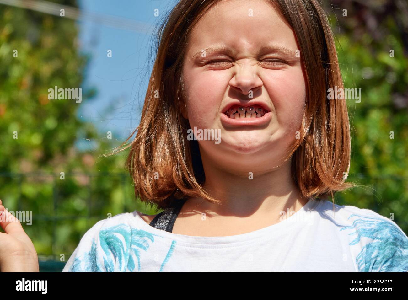 A young girl makes a funny face. Her eyes are closed and her mouth wide ...