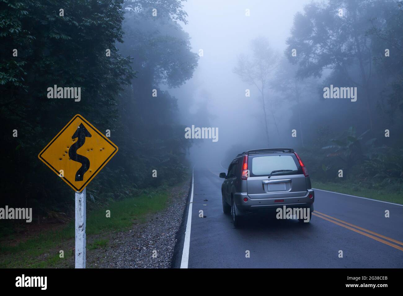 A bullet riddled curvy road sign and silver SUV car on the asphalt road ...