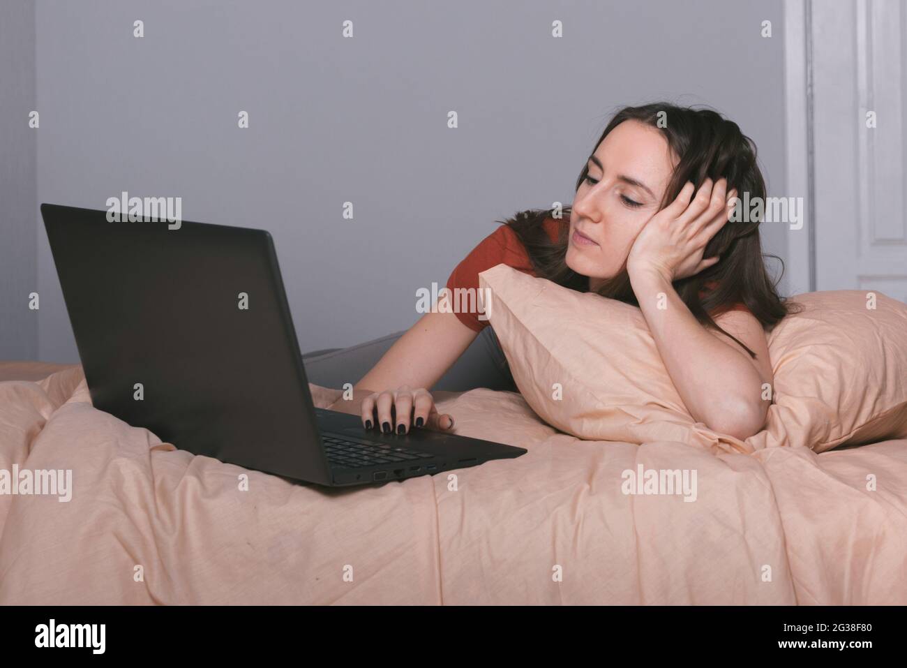 Smiling girl working from home on laptop computer while lying on bed ...