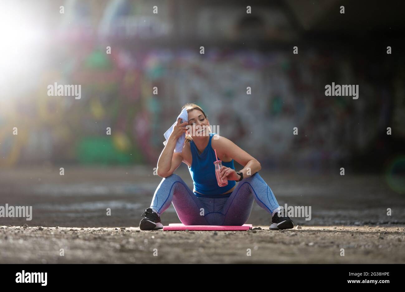 Female athlete sitting on mat resting after exercise in front of wall ...