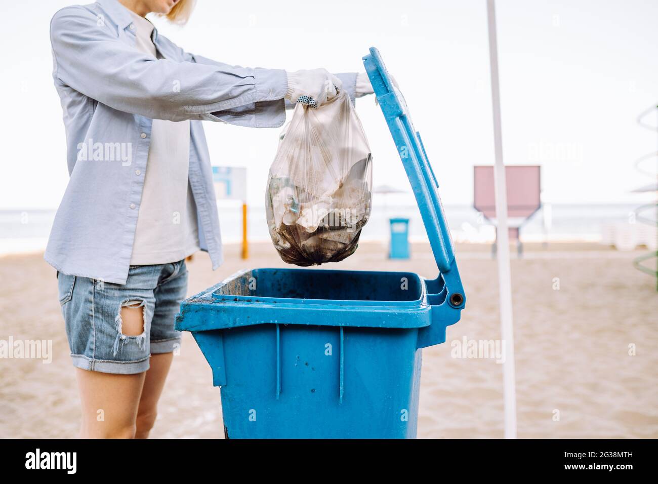 Young female volunteer throws garbage bag into trash can on beach Stock ...