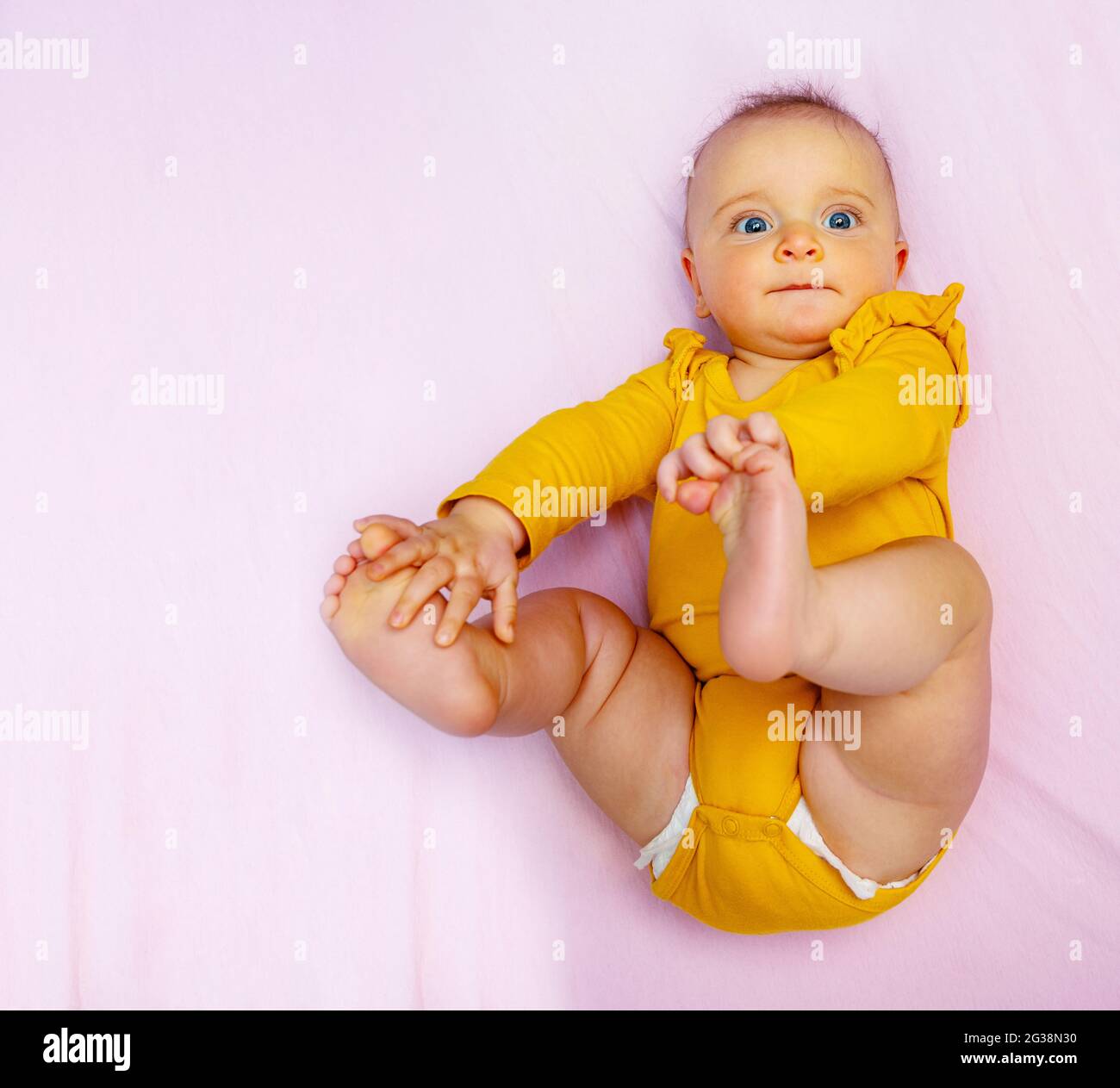 Cute baby girl laying on the pink sheet hold legs Stock Photo - Alamy