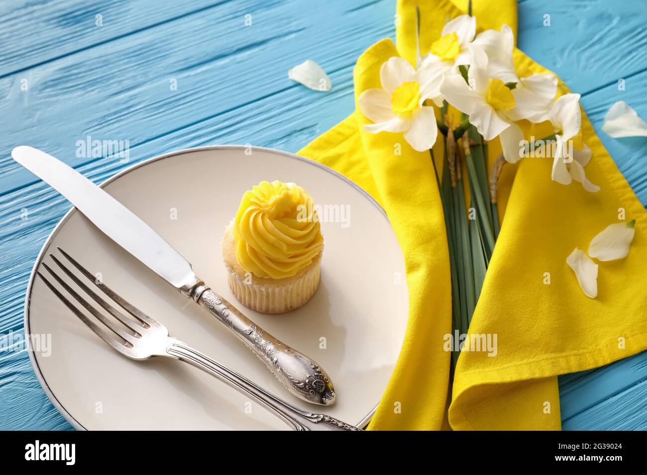 Beautiful table setting with narcissus flowers and cupcake on color ...