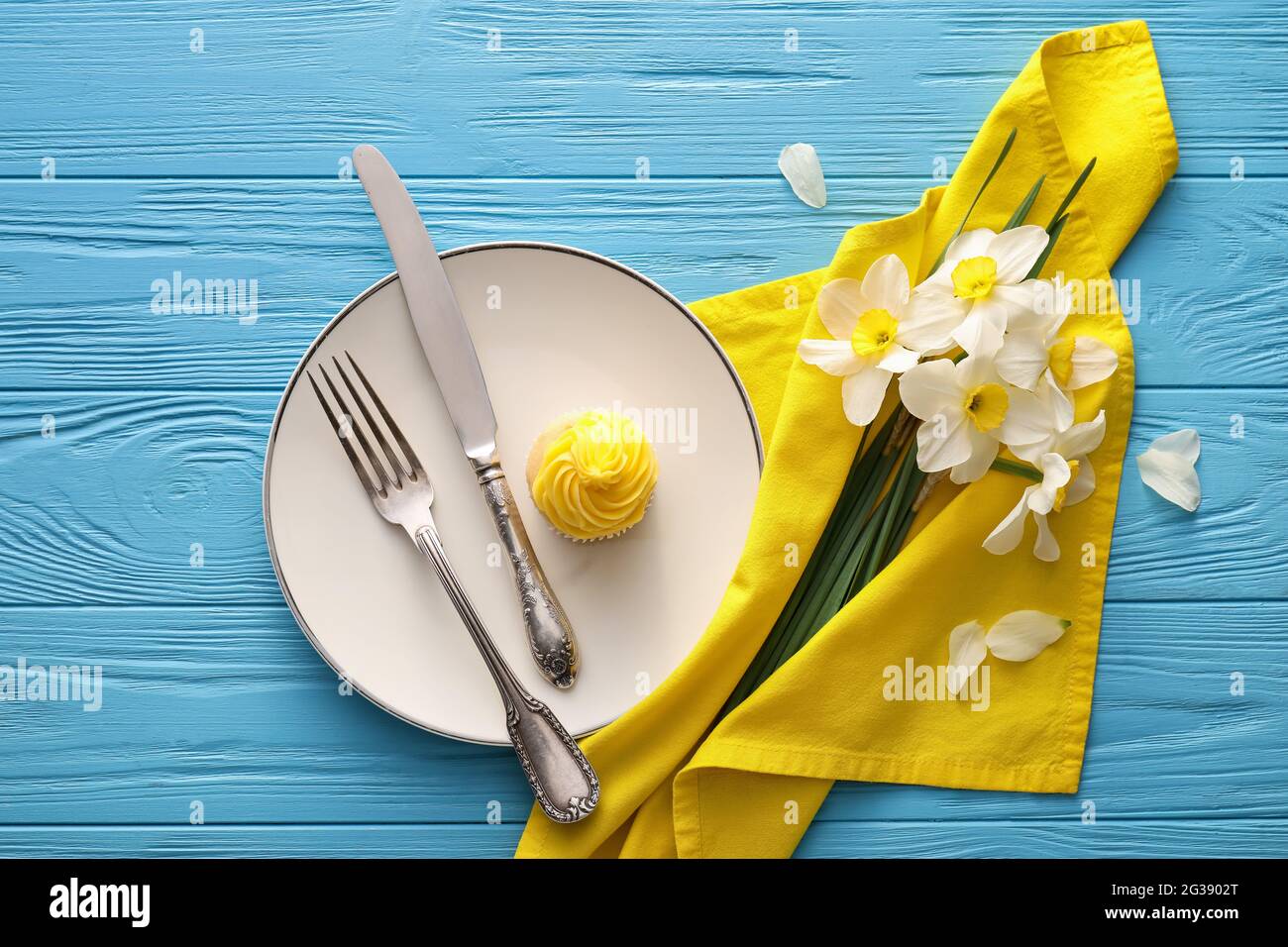 Beautiful table setting with narcissus flowers and cupcake on color ...
