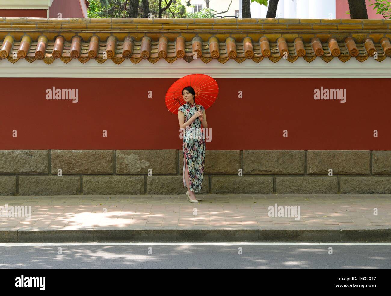 A woman with a parasol poses for a photograph in a Qipao dress by an ...